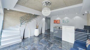 Área de recepção de hotel com piso de mármore, escada, balcão de atendimento e um lustre.