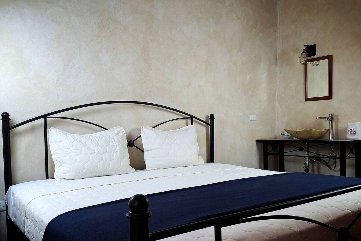Uma cama de solteiro com cabeceira, mesa de cabeceira com espelho e luminária fixada na parede.