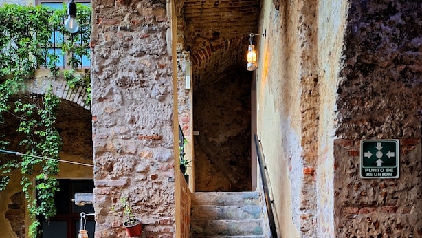 Uma escadaria de pedra estreita que leva a um nível superior, com uma placa indicando um ponto de encontro.
