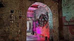 Uma porta em arco que dá para um espaço com parede de pedra, um portão de metal e um banco.