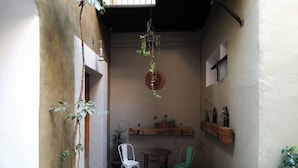 Uma pequena área de pátio com uma planta em vaso, duas cadeiras, uma mesa pequena e um lustre pendurado.