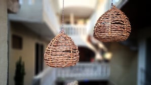 Duas luminárias pendentes de vime em um corredor, com um fundo desfocado de fachada de prédio.