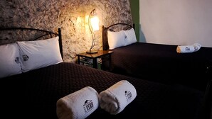Quarto de hotel com duas camas, parede de pedra, parede verde de destaque, luminária pendente e mesa de cabeceira com abajur.