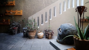 Um pátio com plantas em vasos, uma escultura de pedra e um banco de madeira.