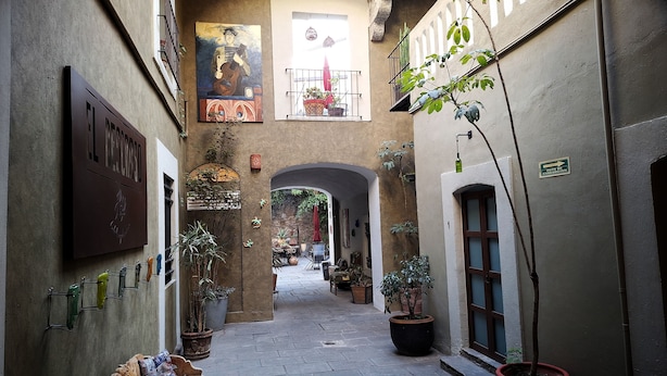 Um beco estreito com um edifício rústico, plantas em vasos e um mural na parede.