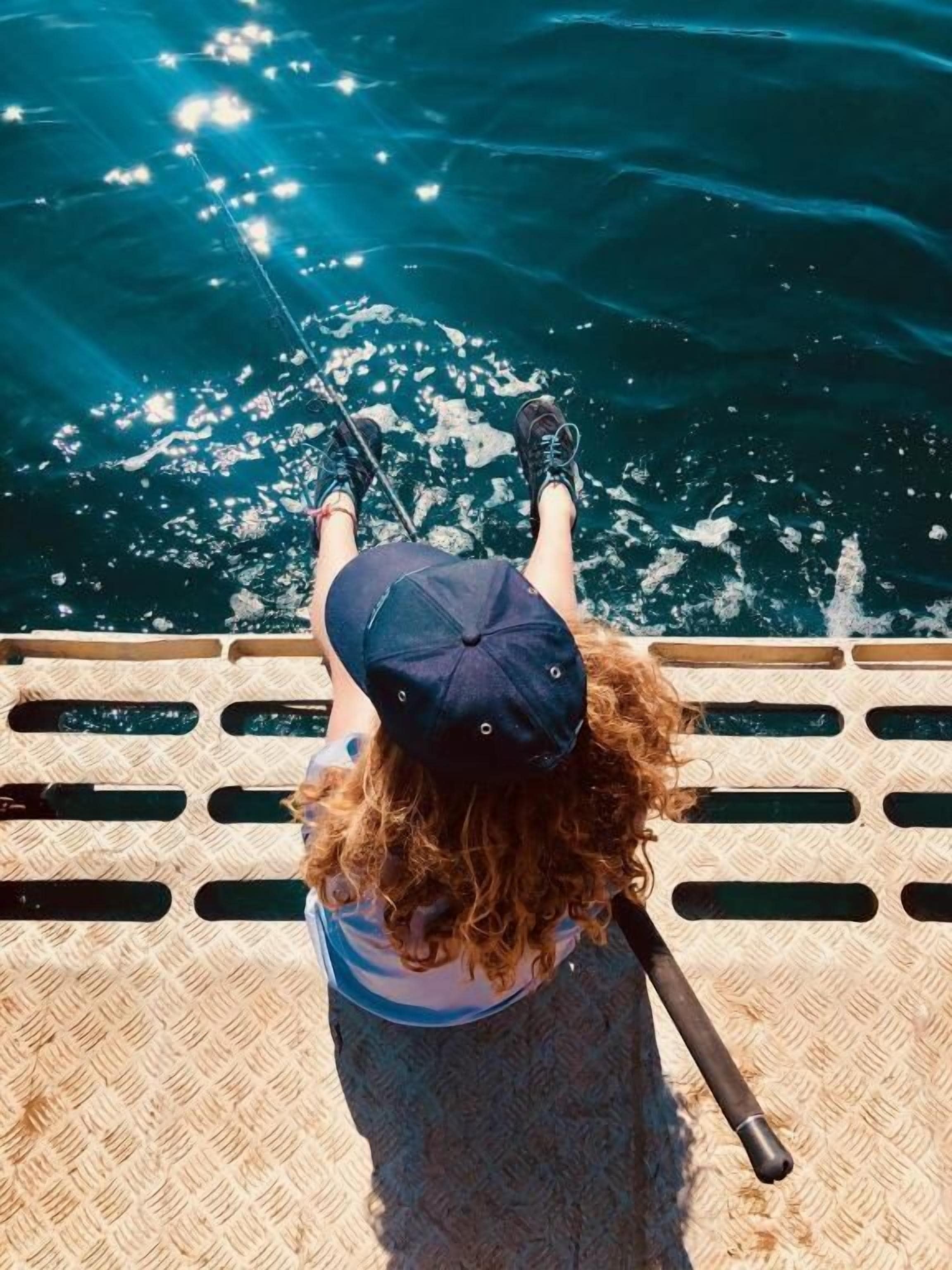 Uma pessoa sentada num cais com uma vara de pesca, contemplando a água.