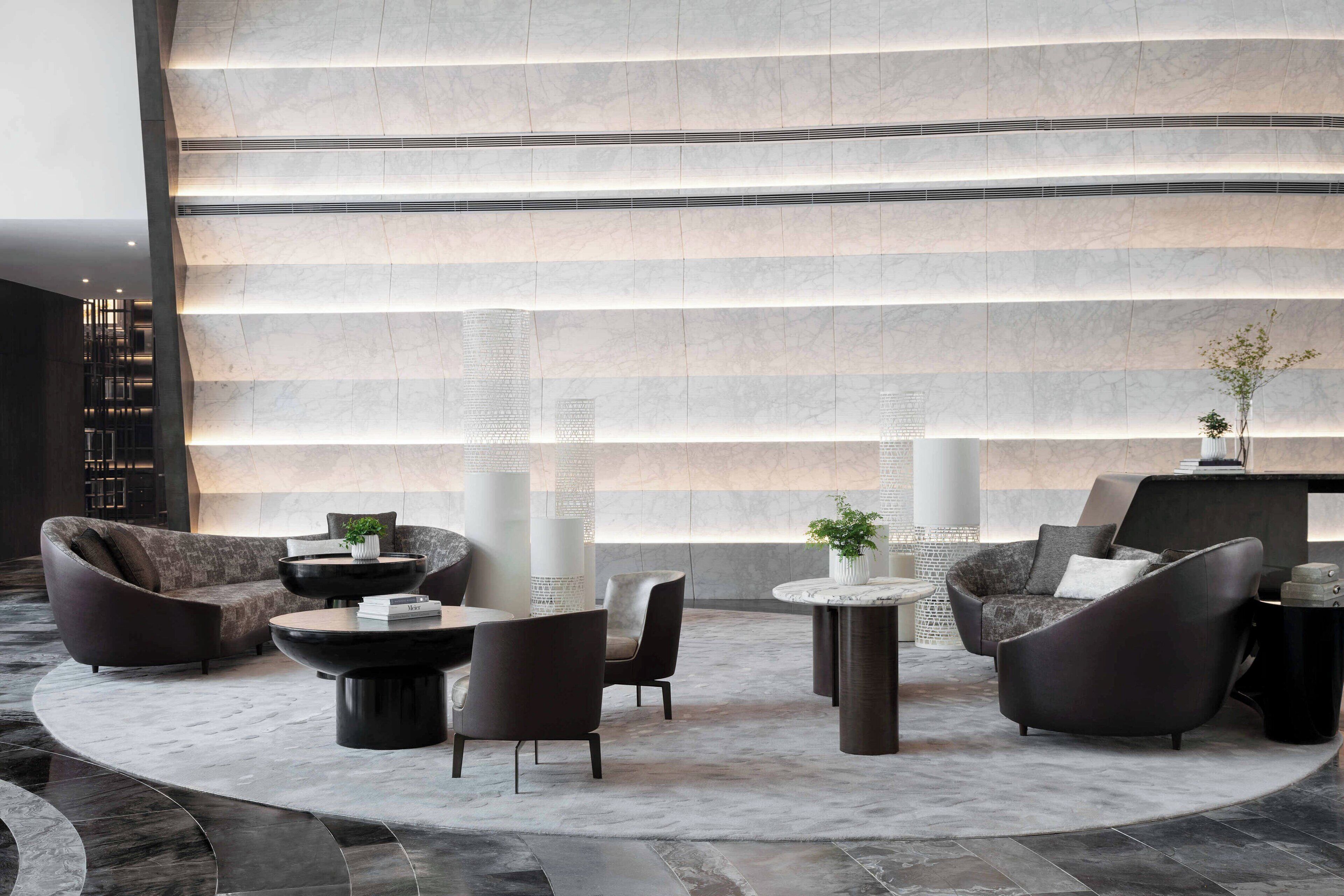 Um lobby moderno com área de estar sinuosa, piso de mármore e uma parede grande com iluminação integrada.
