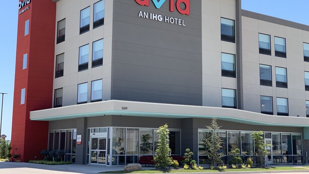 Um Avid An IHG Hotel com fachada moderna, grande entrada de vidro e parede de destaque vermelha.