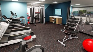 Uma academia com esteiras, máquinas de musculação e uma TV fixada na parede.