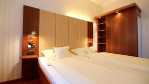 Quarto de hotel com cama grande, guarda-roupa e mesa de cabeceira com abajur.