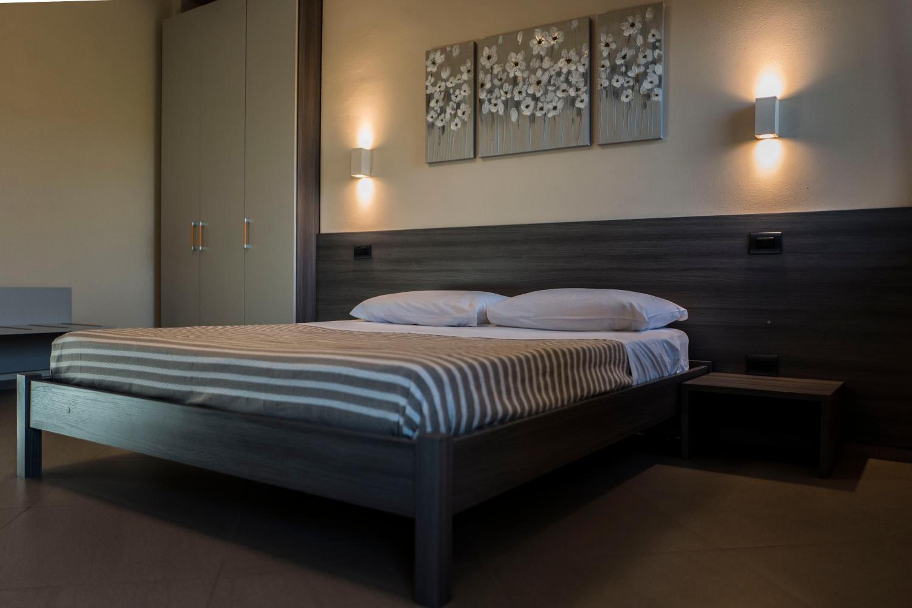 Quarto moderno com cama grande, guarda-roupa e luminárias fixadas na parede.