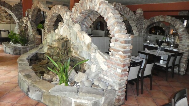 Um restaurante com arcos de pedra, azulejos de barro e um espelho d'água central.