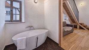 Um banheiro moderno com uma banheira independente, uma janela e uma escada que leva a uma sala de estar.