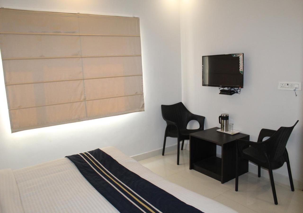 Um quarto com uma cama, uma escrivaninha, duas cadeiras, uma televisão e uma janela com persianas.