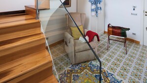 Interior moderno com escada de madeira, guarda-corpo de vidro, piso estampado, sofá e uma pintura na parede.