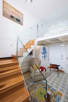 Interior moderno com escada de madeira, guarda-corpo de vidro, piso estampado, sofá e uma pintura na parede.