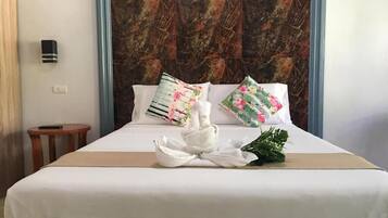 Cama bem arrumada com colcha branca e almofadas decorativas, mesa de cabeceira de madeira com abajur e luminária fixada na parede.