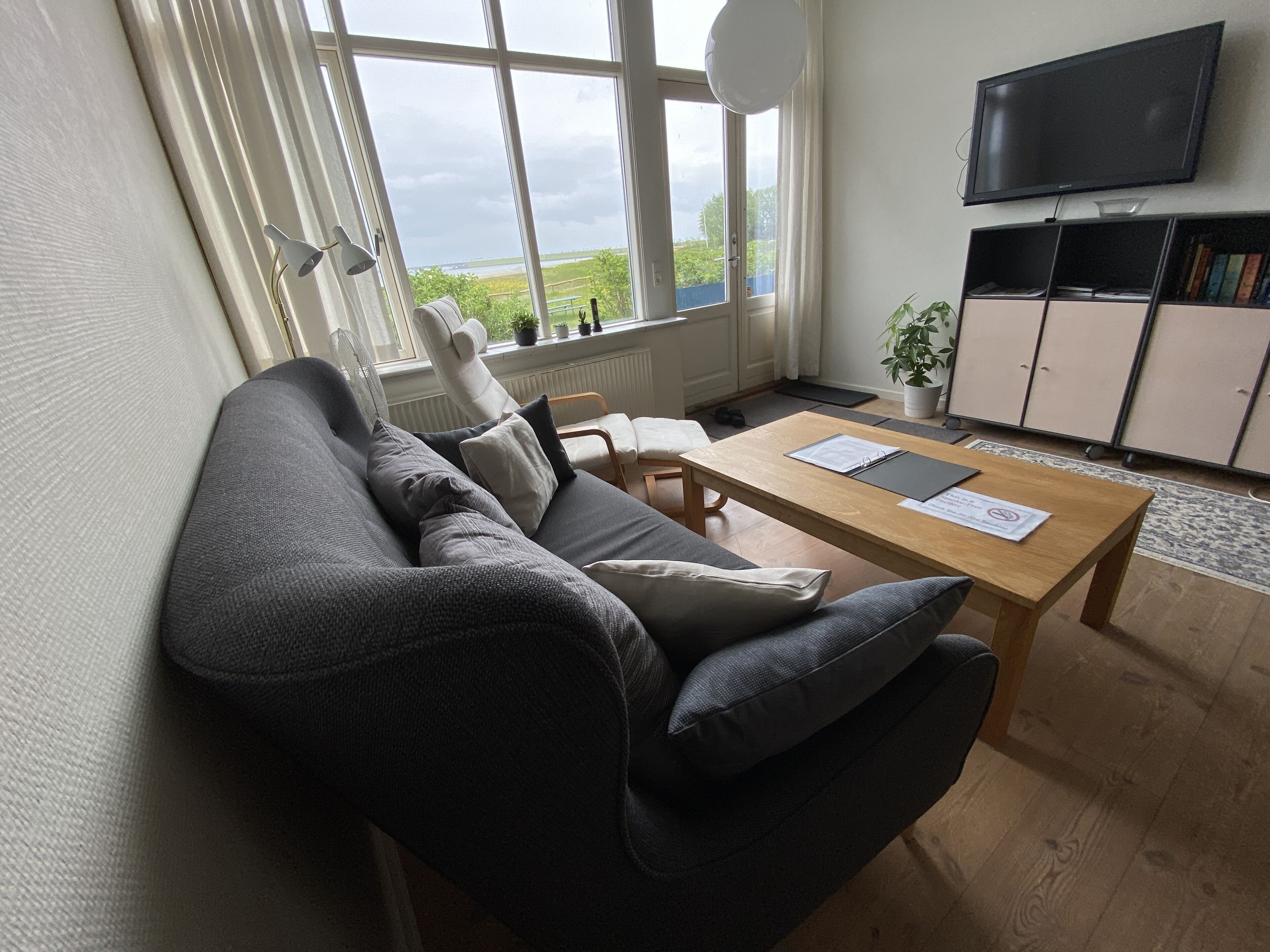 Uma sala de estar moderna com um sofá, uma mesa de centro de madeira e uma TV fixada na parede.