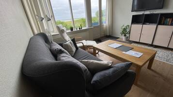 Uma sala de estar moderna com um sofá, uma mesa de centro de madeira e uma TV fixada na parede.