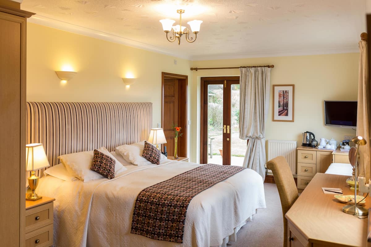 Quarto de hotel com uma cama grande, luminárias de cabeceira, uma escrivaninha com cadeira, televisão e uma janela com cortinas.