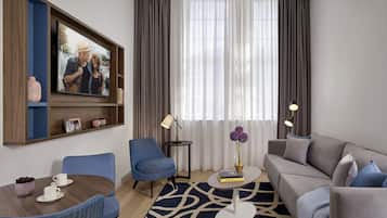 Uma sala de estar moderna com sofá, poltronas, mesa de centro, televisão e uma janela grande com cortinas.