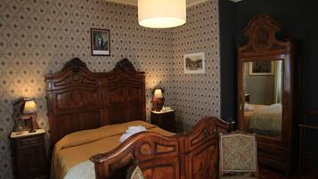 Quarto tradicional com cama de madeira, duas mesas de cabeceira com abajures, um espelho e papel de parede estampado.