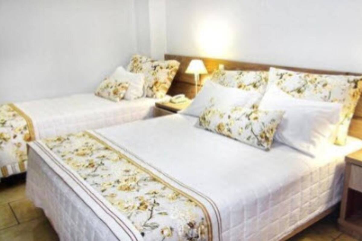 Quarto de hotel com duas camas de solteiro, cada uma com roupa de cama florida e almofadas combinando. Há mesas de cabeceira com abajures e uma mesinha de cabeceira de madeira com uma gaveta.