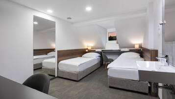 Quarto de hotel moderno com duas camas de solteiro, uma escrivaninha, uma cadeira, um espelho grande e um banheiro com pia.