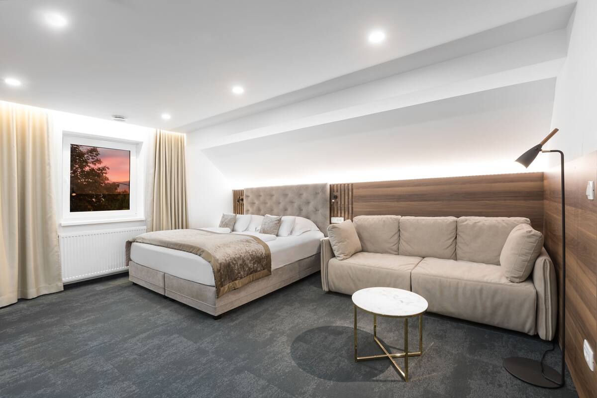 Quarto moderno com cama, sofá, uma mesinha e janela com cortinas.