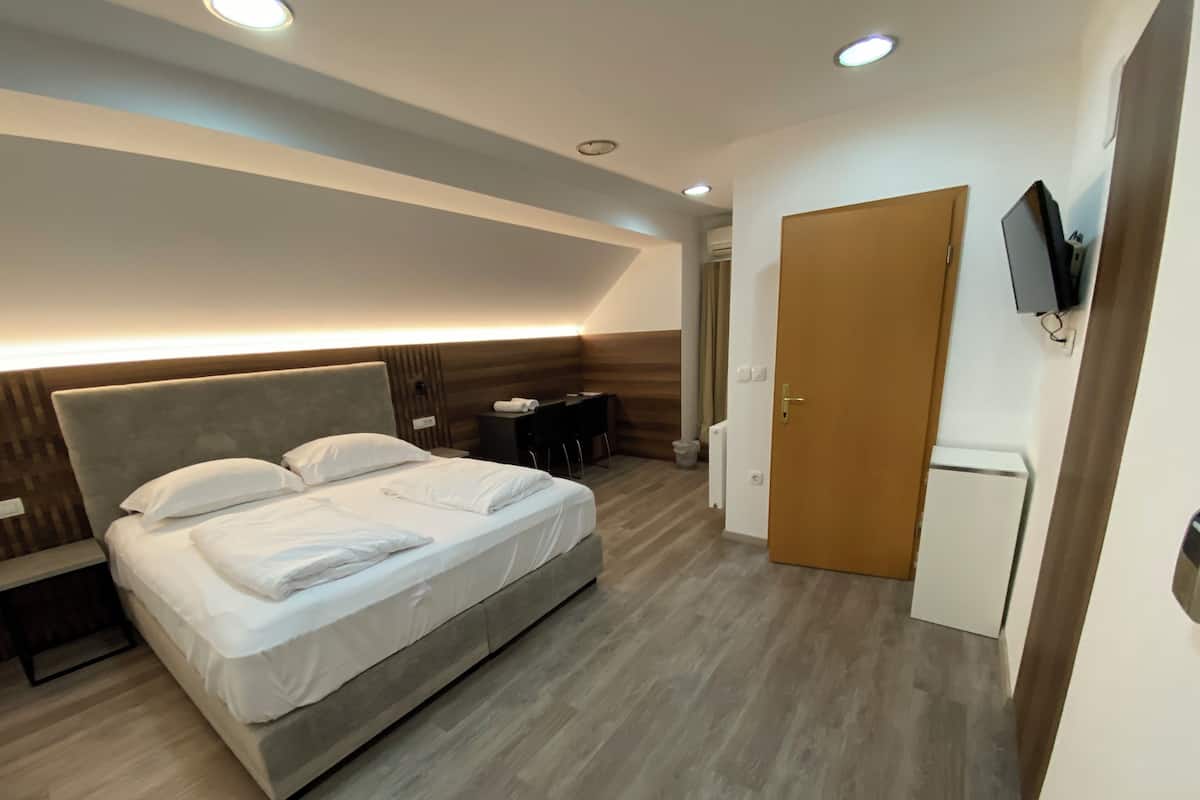 Quarto de hotel moderno com uma cama grande, uma escrivaninha, uma cadeira, televisão na parede e uma porta.