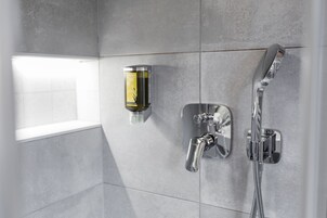 Um banheiro moderno com chuveiro, dosador de sabonete e janela que permite entrada de luz natural.
