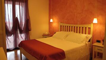 Quarto de hotel com cama, mesa de cabeceira, luminária e janela com cortinas.