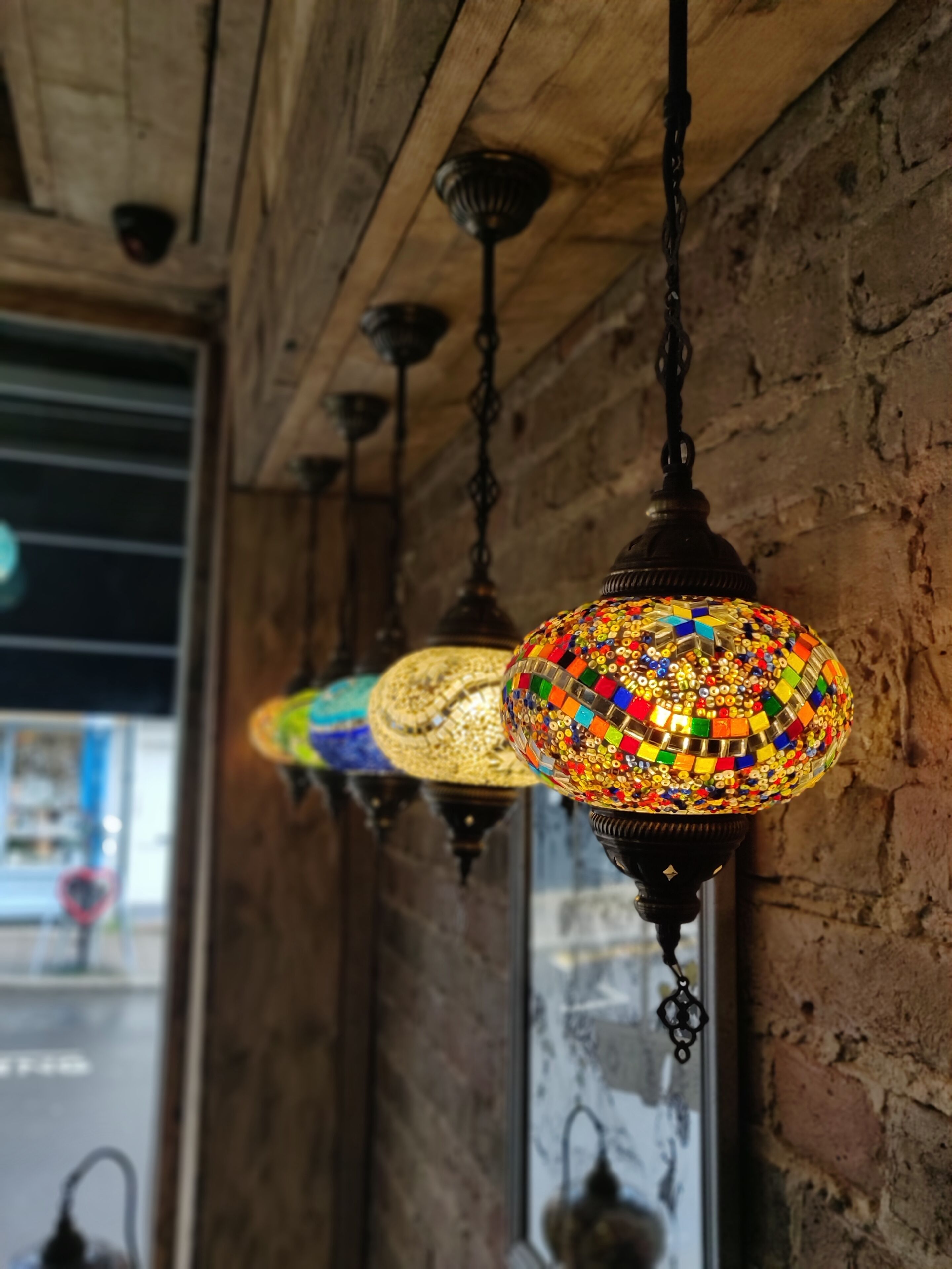 Fileira de luminárias decorativas penduradas com padrões de mosaico, suspensas de um teto de madeira em ambiente rústico.