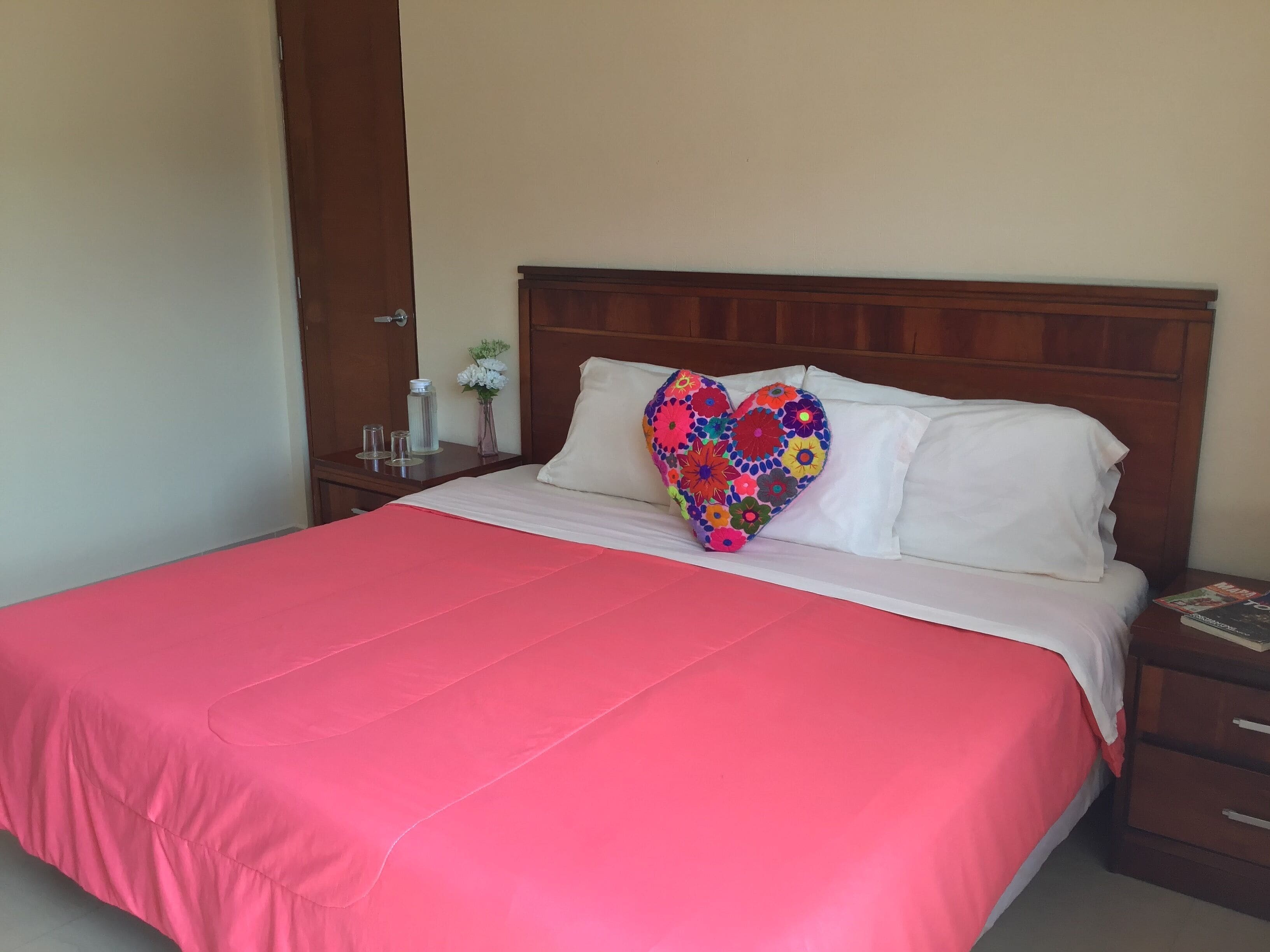 Uma cama bem arrumada com um edredom rosa, um travesseiro em formato de coração e uma cabeceira de madeira.