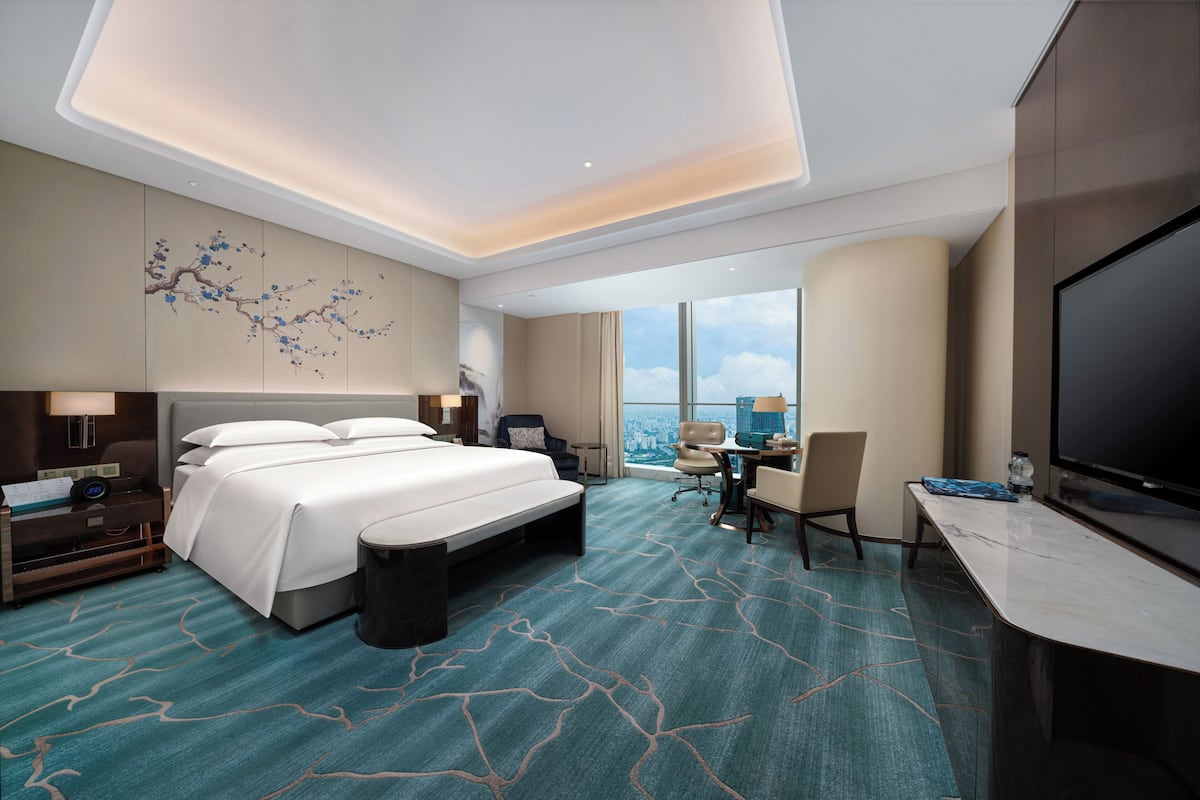 Quarto de hotel com cama grande, escrivaninha, cadeira, televisão e vista para a cidade.