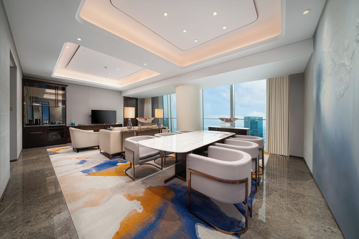 Quarto de hotel moderno com uma grande mesa de jantar, assentos confortáveis, uma televisão de tela plana e vista para a cidade.