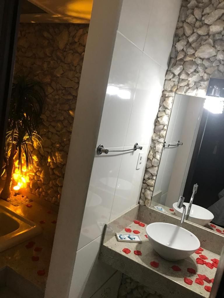 Casa de banho com parede de pedra, lavatório branco e espelho.