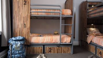 Quarto com beliches, painéis de madeira, compartimentos de armazenamento numerados e uma mochila azul.