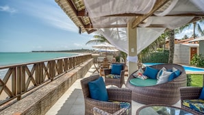 Uma área de estar coberta ao ar livre com móveis de vime, piscina e vista para o mar.