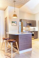Uma cozinha moderna com ilha central, banquetas, micro-ondas e pia.