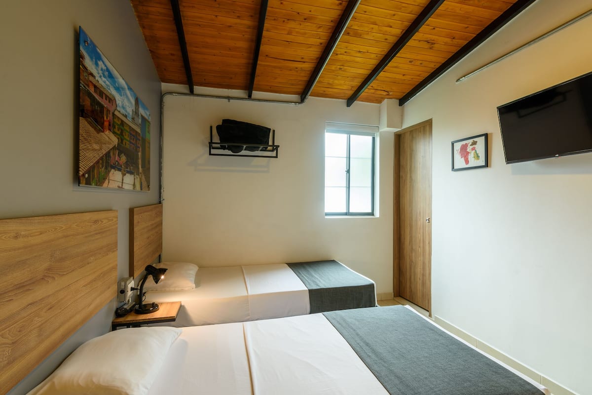 Quarto com duas camas, teto de madeira, televisão e janela.