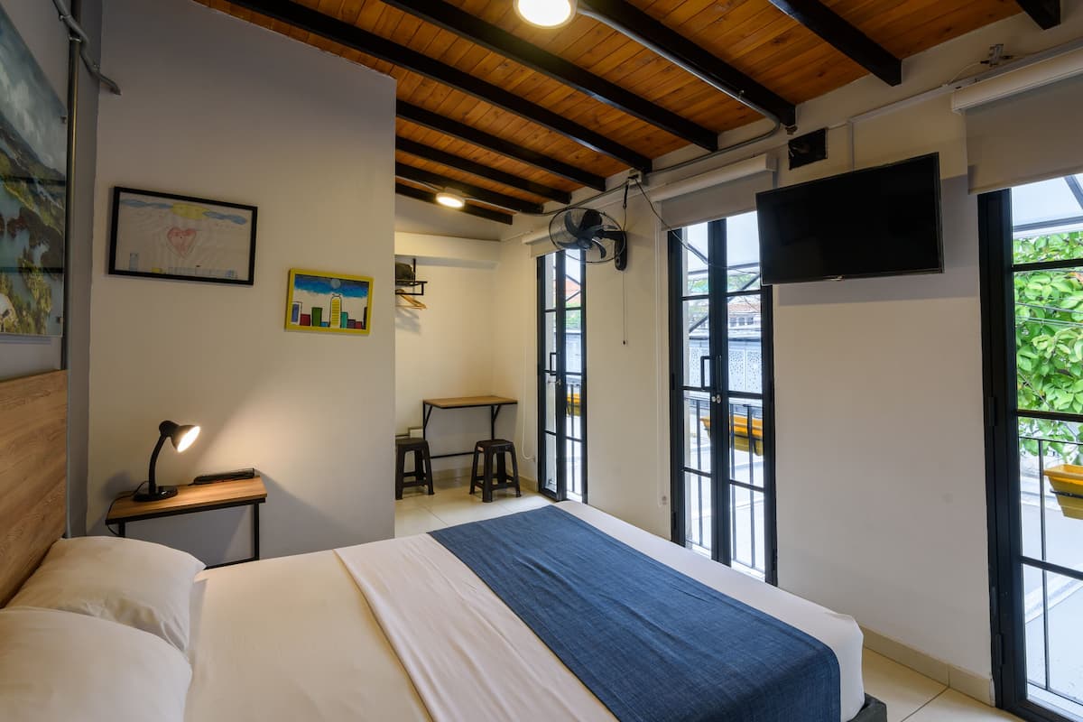 Quarto com cama, escrivaninha, cadeira, ventilador e televisão.