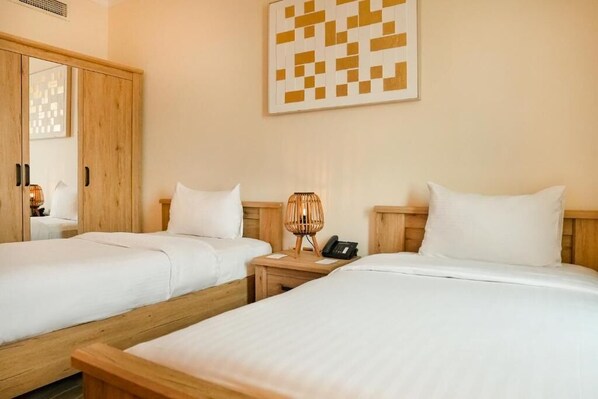 Quarto de hotel com duas camas de solteiro, cabeceiras de madeira, mesa de cabeceira com abajur e um espelho grande.