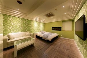 Quarto com cama, mesinha de centro de vidro, sofá branco e parede com padrão verde.