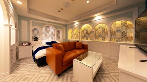 Quarto de hotel moderno com uma cama grande, um sofá, uma mesa de centro de vidro e painéis decorativos na parede.