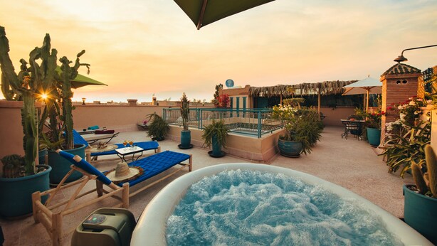 Terraço no terraço com hidromassagem, espreguiçadeiras, plantas em vasos e vista para o pôr do sol.