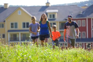 Uma família caminhando em um campo gramado, com casas ao fundo.