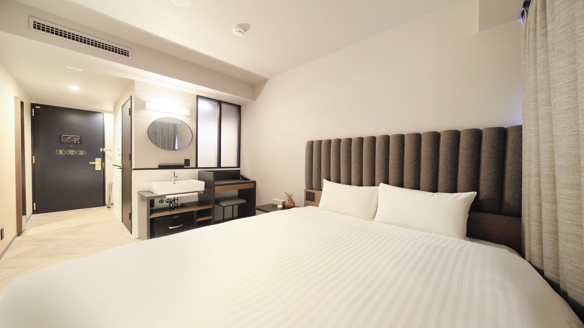 Quarto de hotel com uma cama grande, uma toucador com espelho, uma mesa de escritório e cabeceira com painéis verticais.