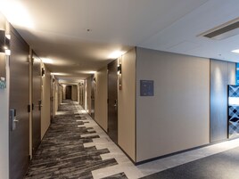 Corredor de hotel com carpete estampado, portas em ambos os lados e uma placa fixada na parede.