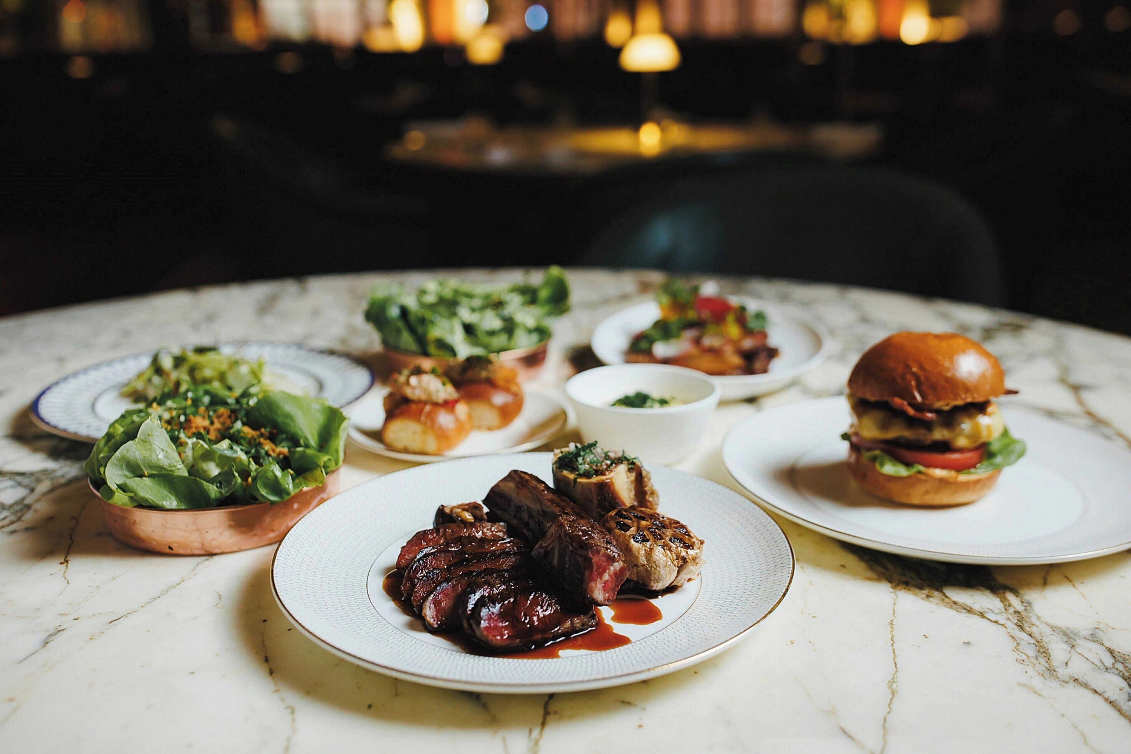 Uma mesa com diversos pratos, incluindo um hambúrguer, bife e salada.